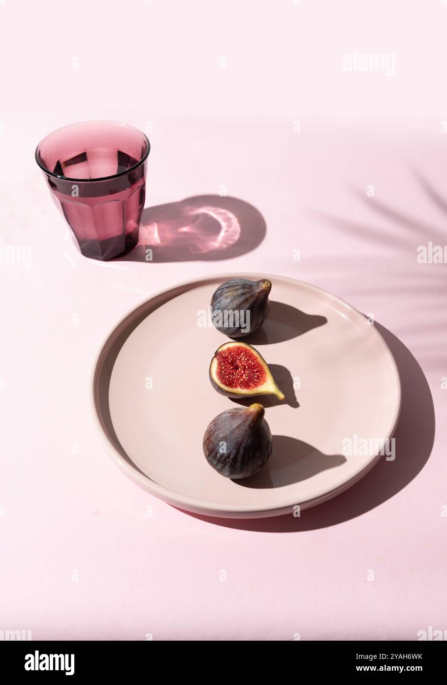 A purple fig cut in half next to two whole figs on a pink plate against ...