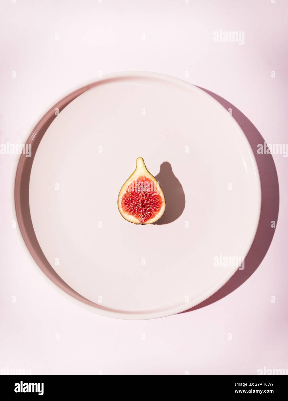 A single half-cut fig reveals its bright red interior, placed on a pink ...