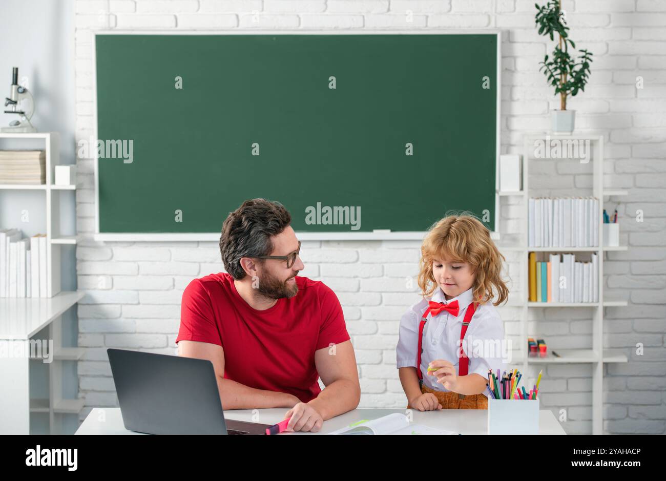Elementary school boy in classroom on lesson. Teacher explaining to ...