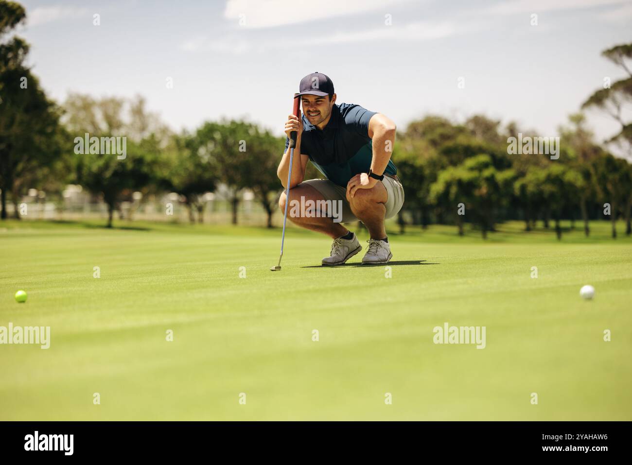 A caucasian man crouches and aims intently on a green golf course ...