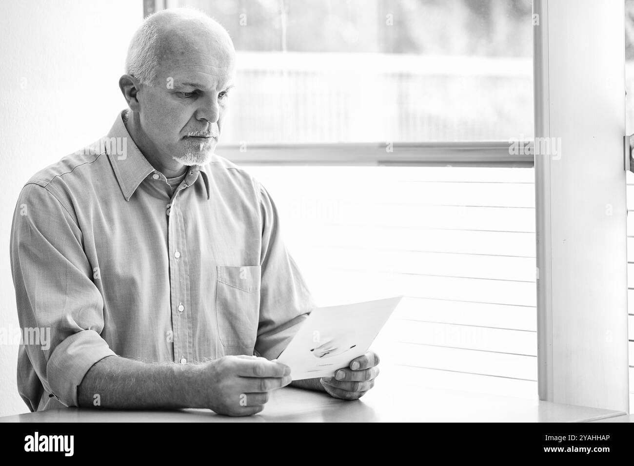 Mature man reads a letter with concern in a home office, reflecting on ...