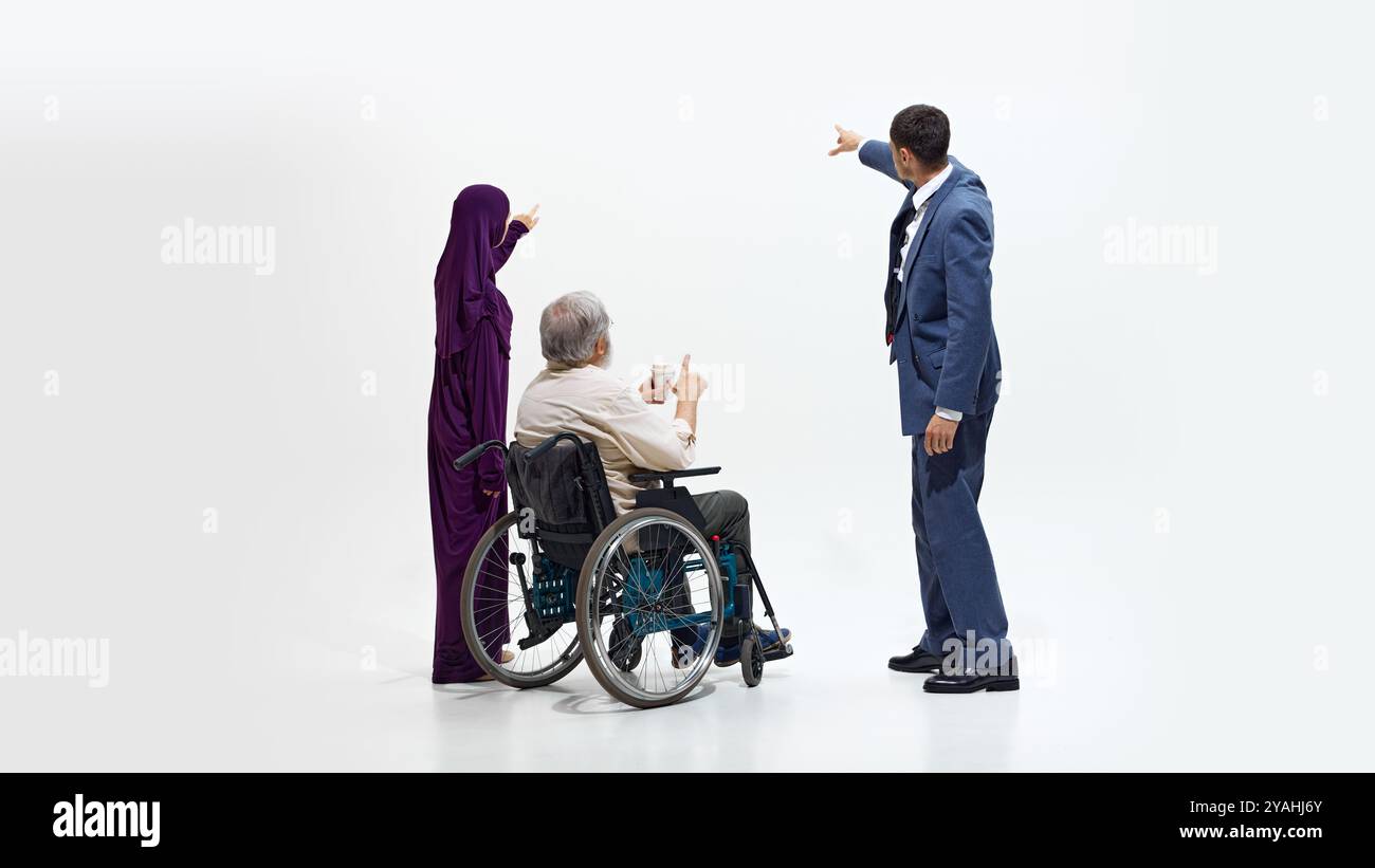 Three people, including man in wheelchair, look forward while pointing ...