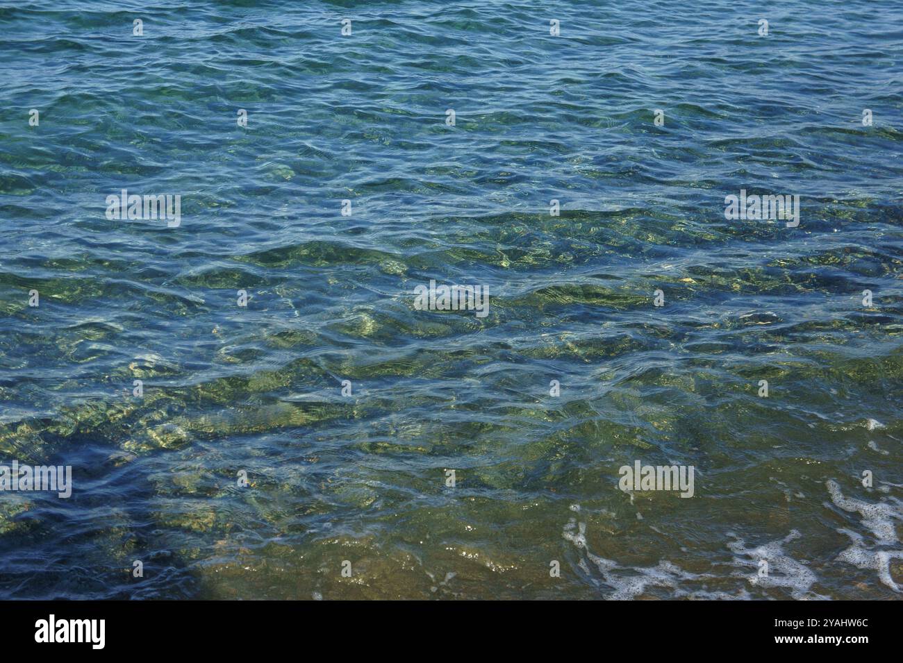 The image shows a close-up of clear blue water gently lapping against ...