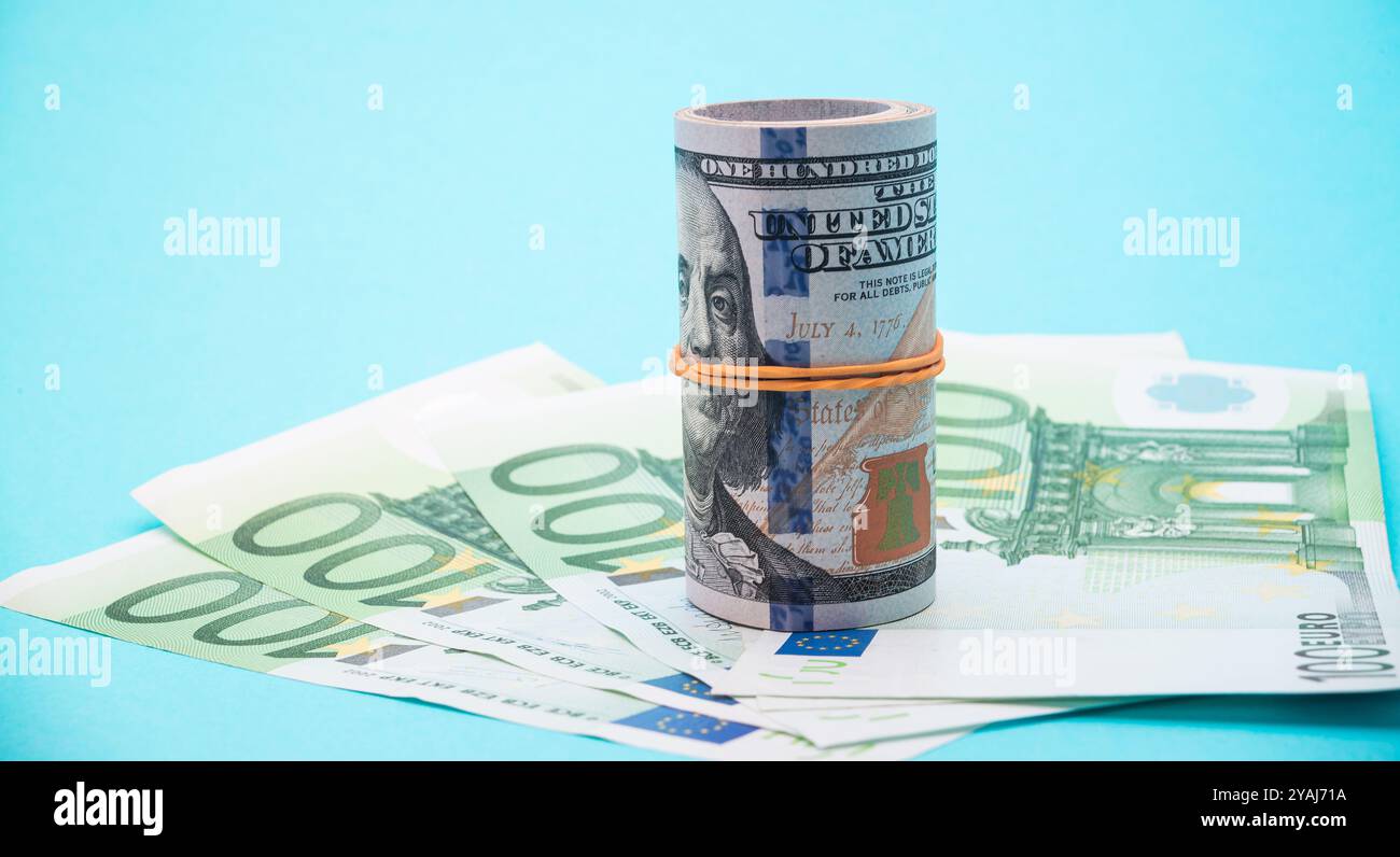 A rolled stack of dollars stands surrounded by fanned out hundred euros ...