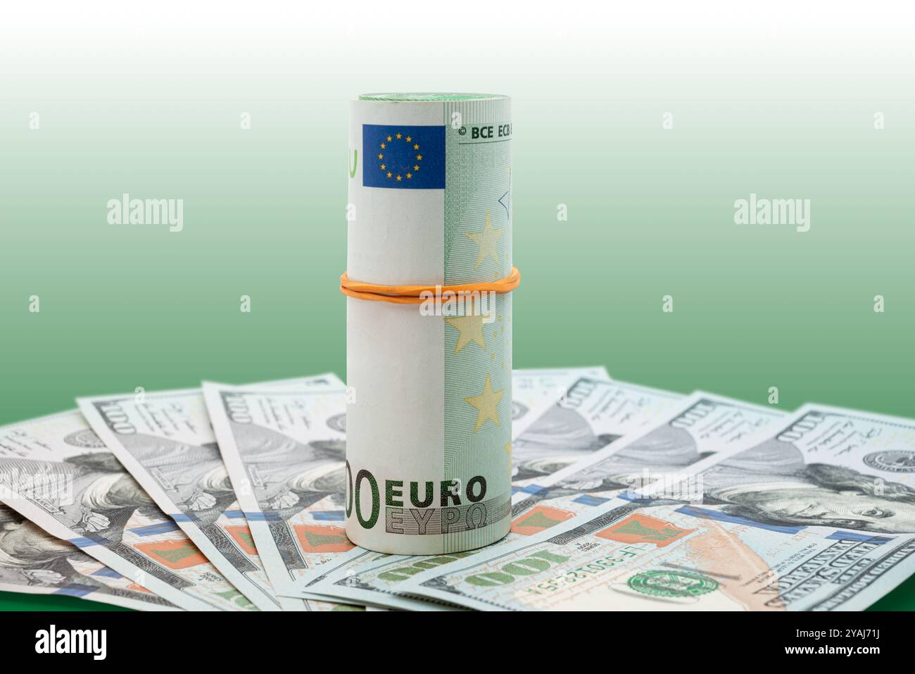 A rolled stack of euros stands surrounded by fanned out hundred dollar ...