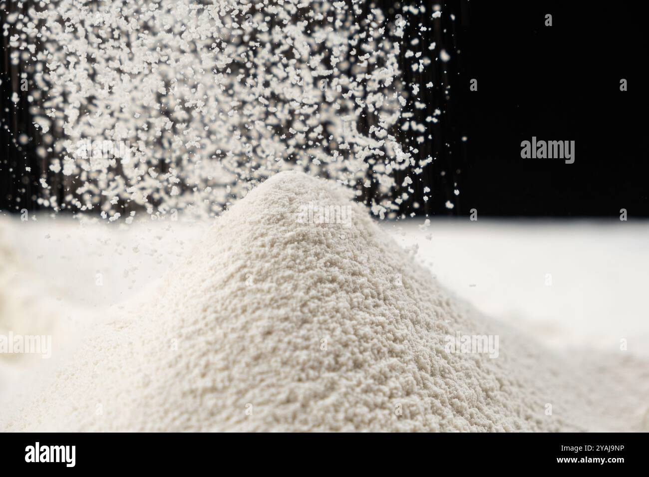 Wheat flour pouring onto a pile on a black background Stock Photo - Alamy
