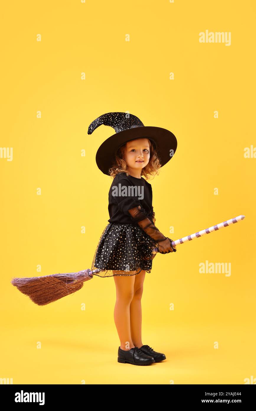 Cute girl with broom dressed like witch on yellow background. Halloween ...