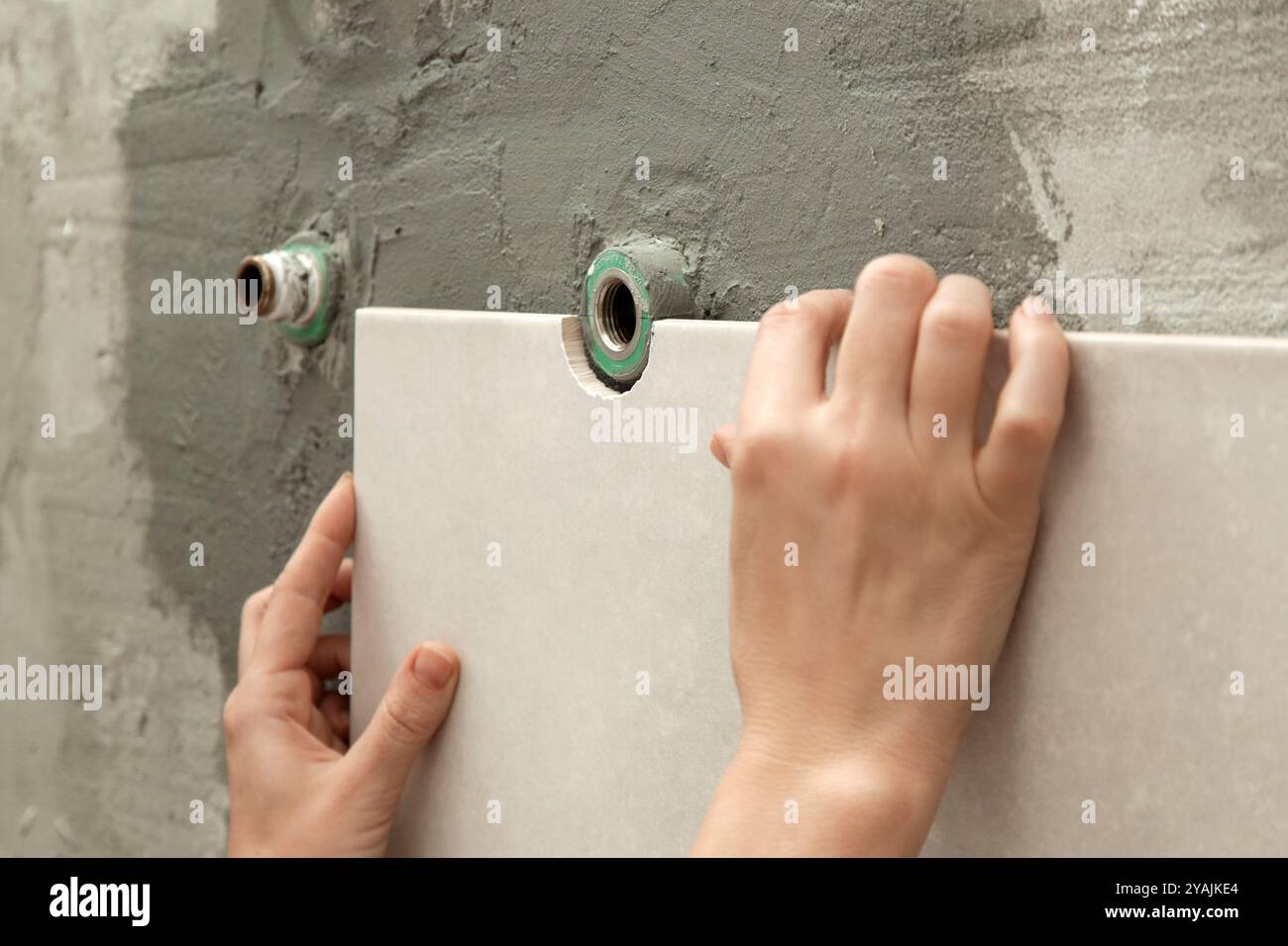 Woman tiling bathroom walls, applying adhesive on a tile and placing ...