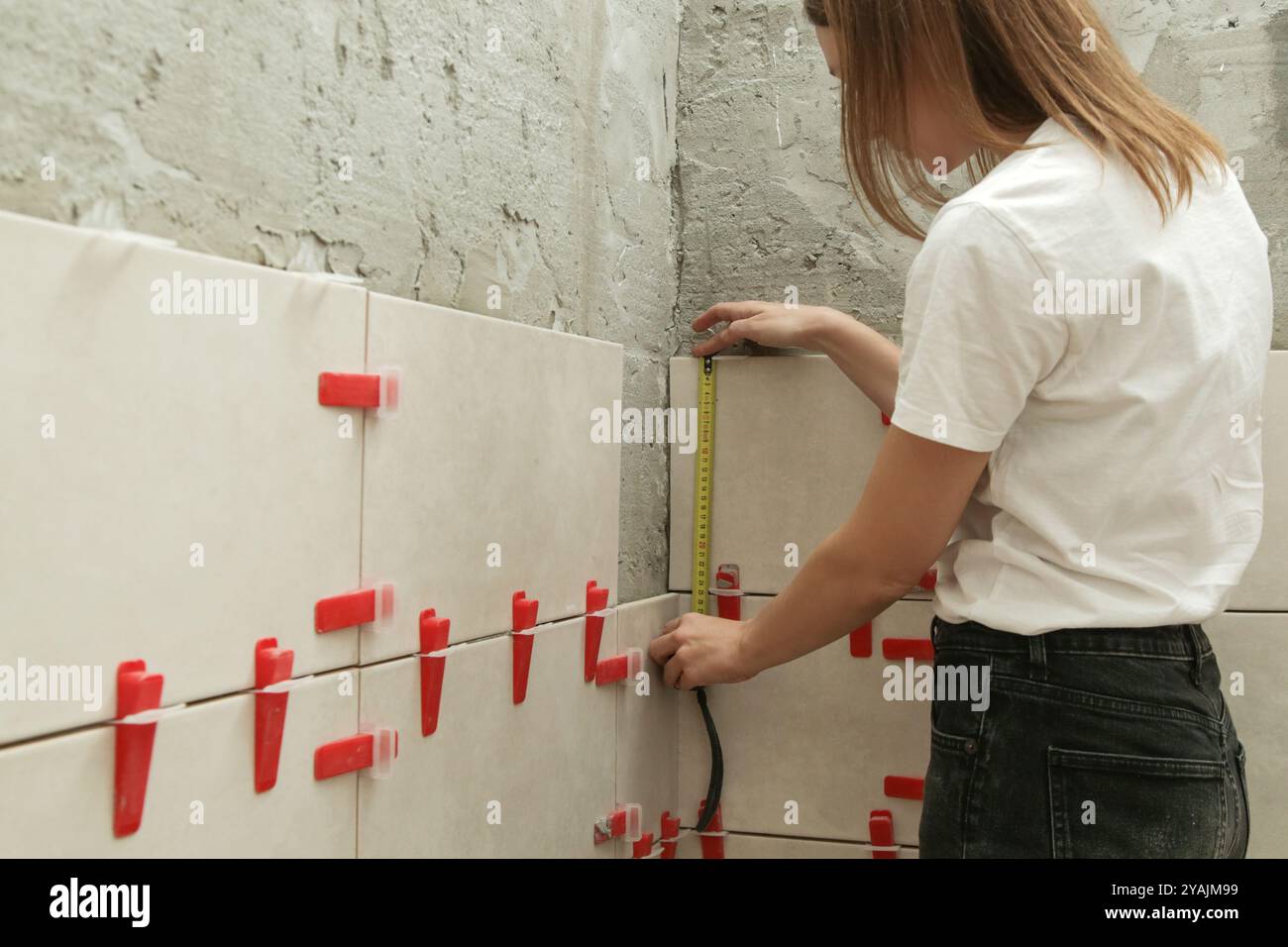Woman tiling bathroom walls, using tape measure for measuring length ...
