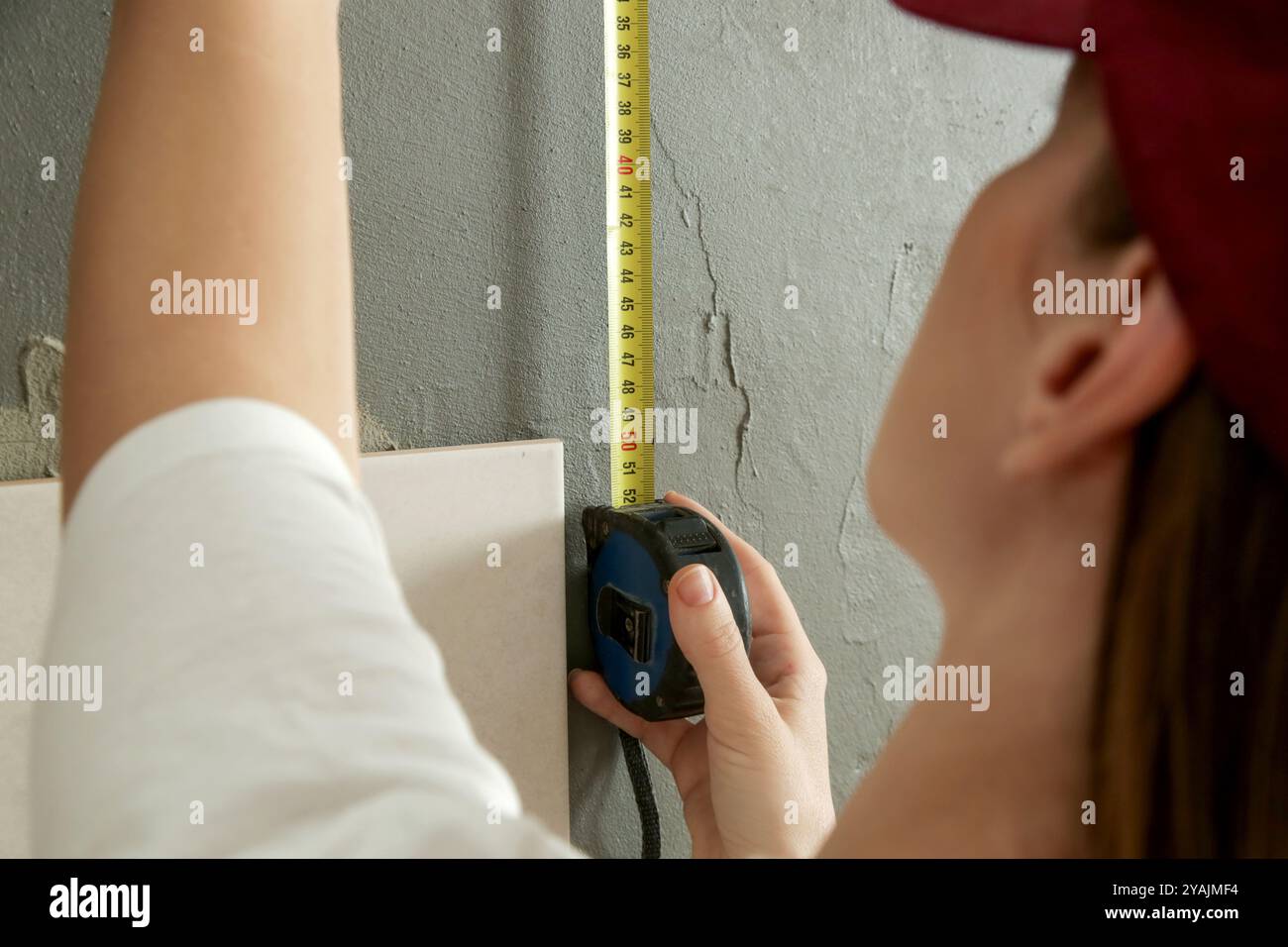 Woman tiling bathroom walls, using tape measure for measuring length ...