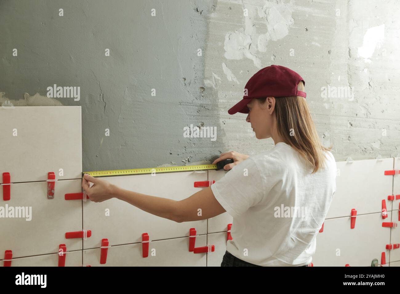 Woman tiling bathroom walls, using tape measure for measuring length ...