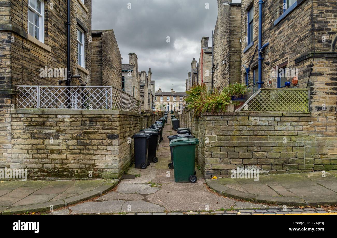 Wheelie bins line the ginnel (alleyway, snicket) between two rows of ...