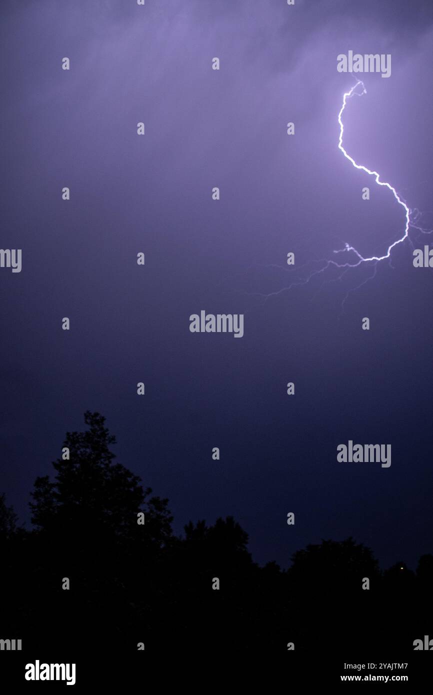 Powerful vertical lightning bolt striking near a solitary tree under a ...