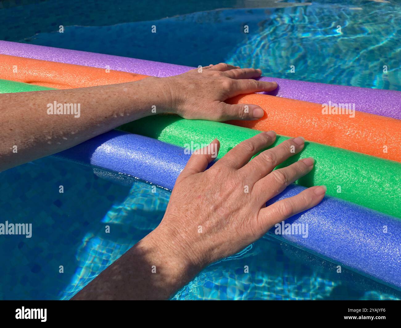 Rainbow coloured floating foam sticks and female hands, in swimming ...
