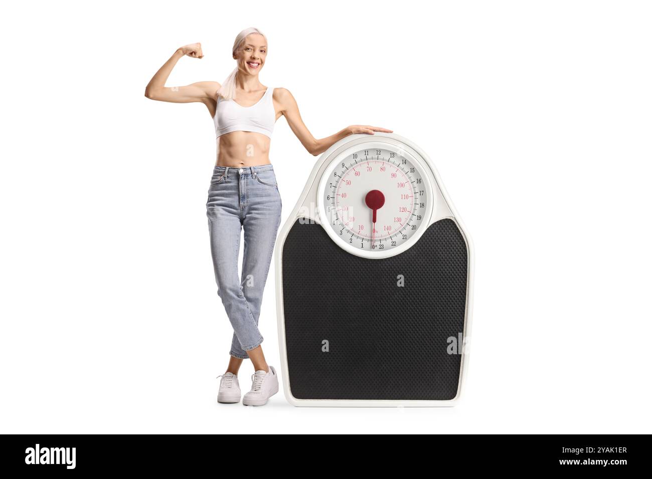 Happy slim woman in jeans and crop top standing next to a weight scale ...
