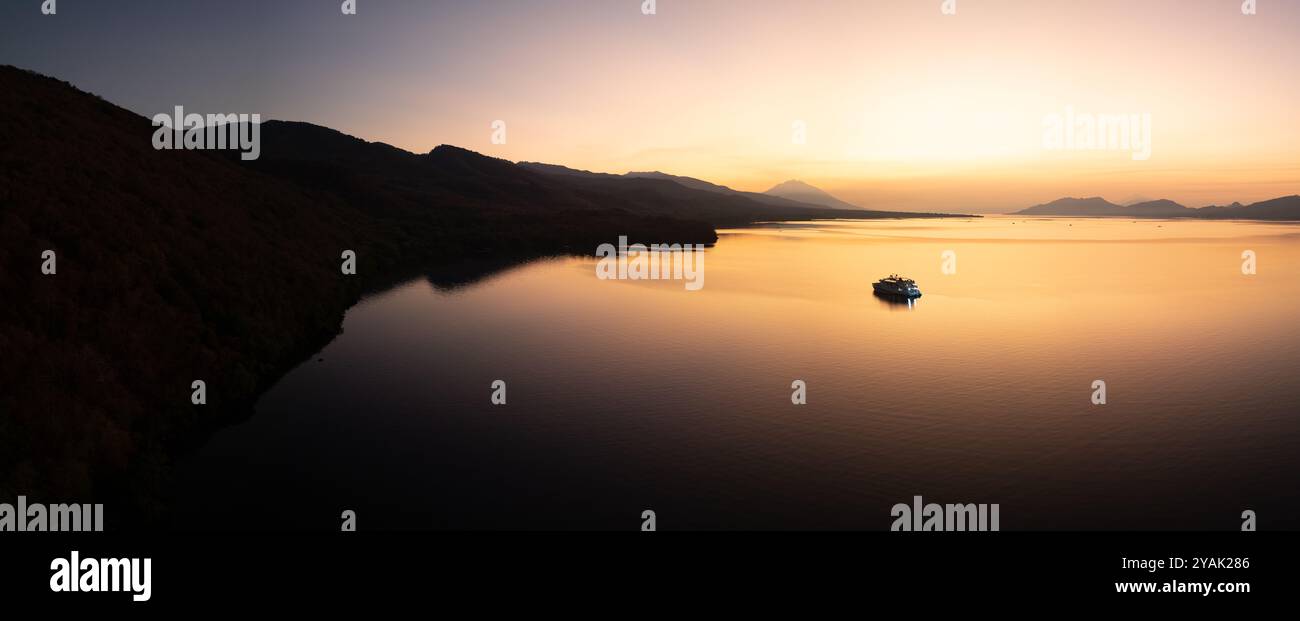 Sunrise silhouettes a small ship near the beautiful island of Adoenara ...