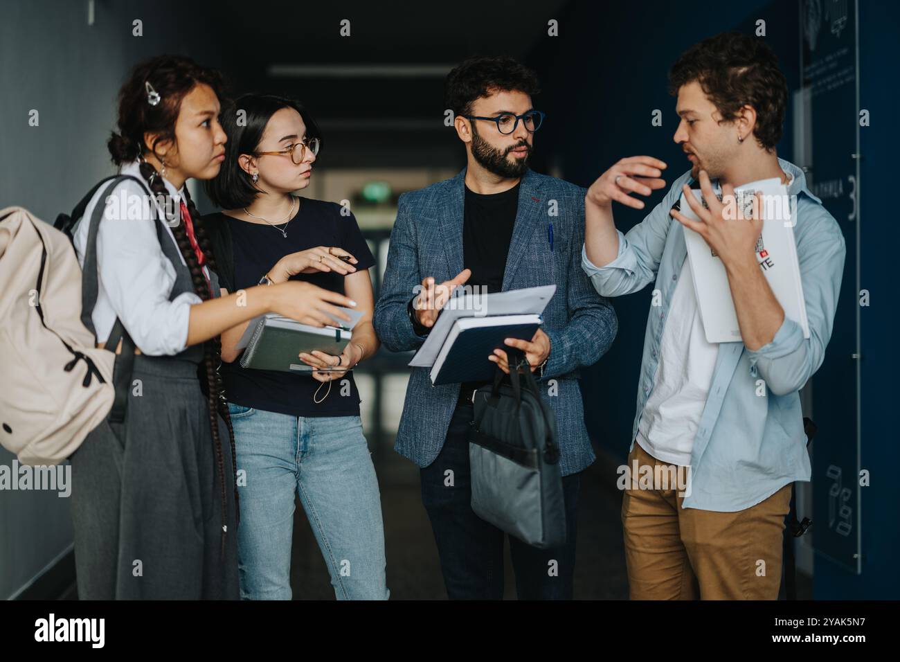Students engaged in discussion with professor in university hallway ...