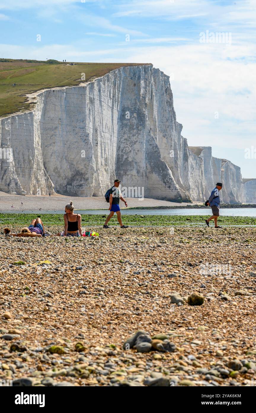 The Seven Sisters with their chalk sea cliffs loom large while two men walk past sunbathing ...
