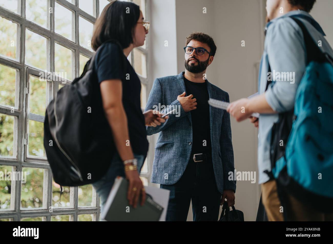 College students engaged in discussion with their professor in hallway ...