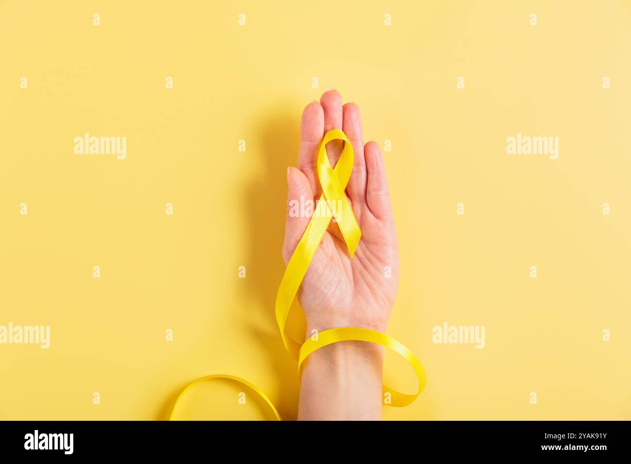Yellow cancer ribbon in womans hand on yellow background Stock Photo ...