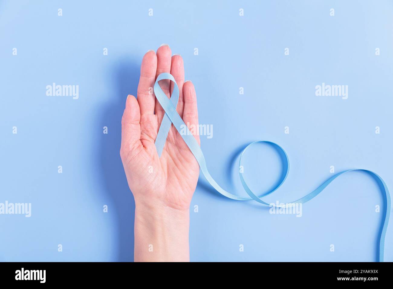 Blue cancer ribbon in womans hand on light blue background Stock Photo ...