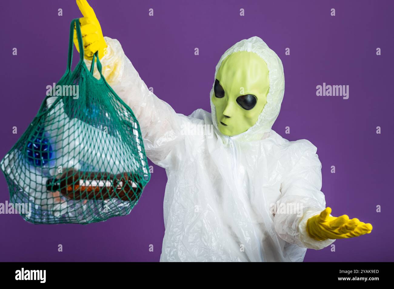Person wearing an alien mask and a hazmat suit is holding a bag of ...