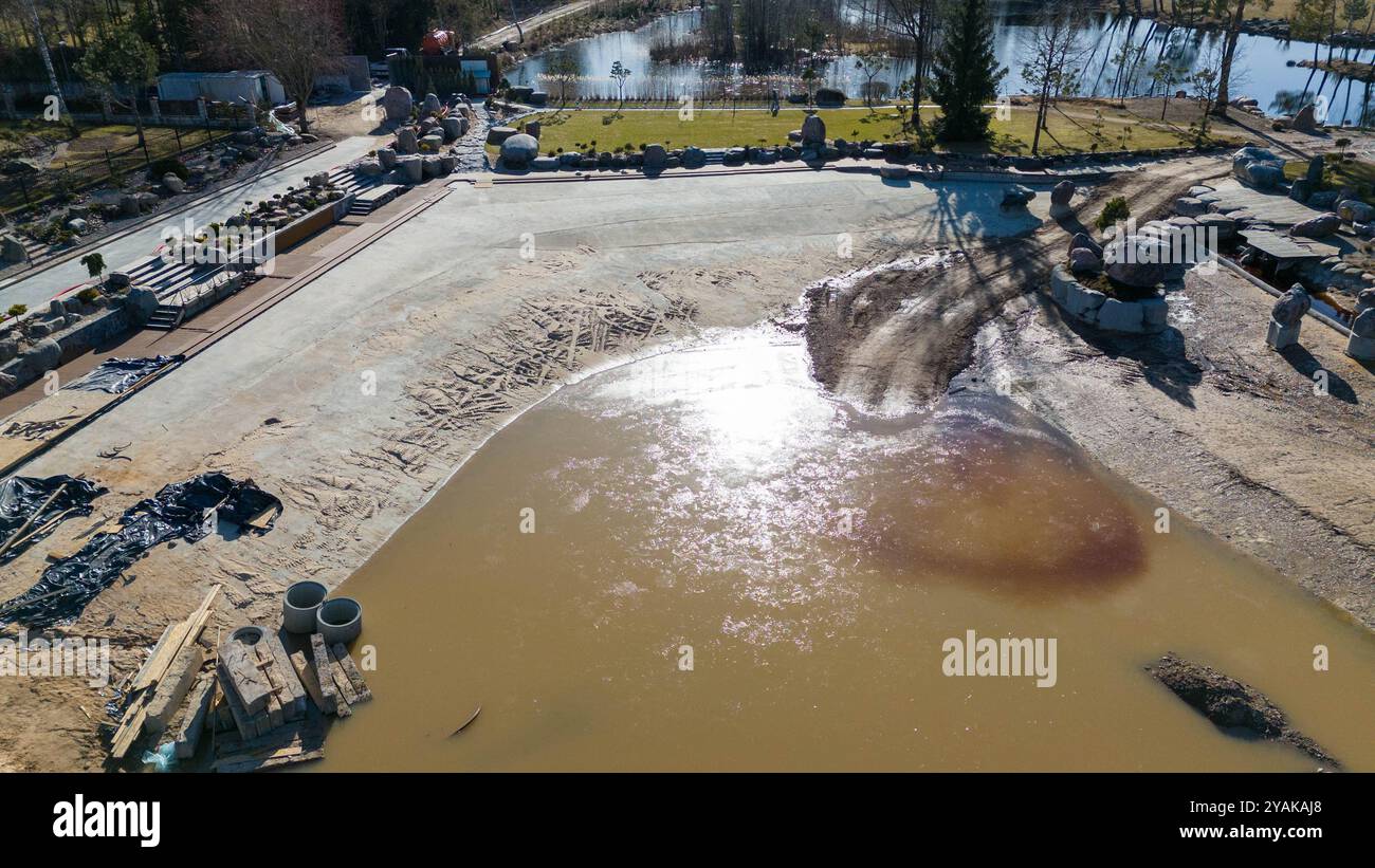 An aerial view of a construction site near a pond. The area shows a mix ...