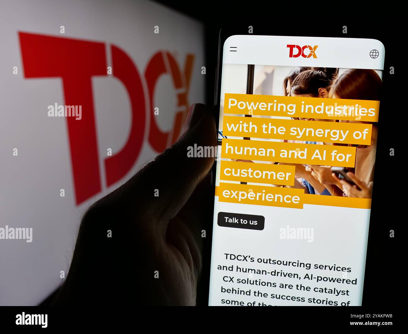 Person holding cellphone with webpage of Singaporean customer experience company TDCX on screen ...
