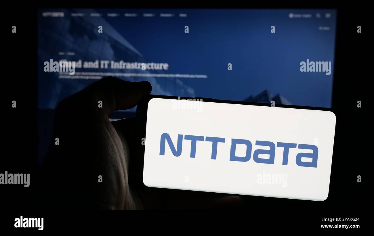 Person holding smartphone with logo of Japanese IT company NTT DATA Corporation on screen in ...