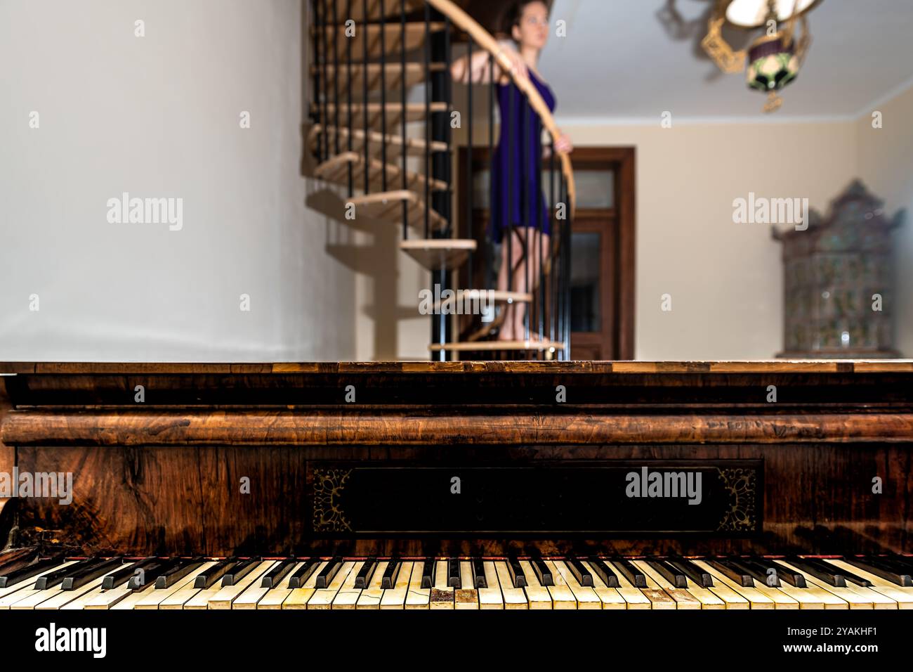 Wooden old-fashioned forte piano with young girl woman pianist walking down spiral stairs ...