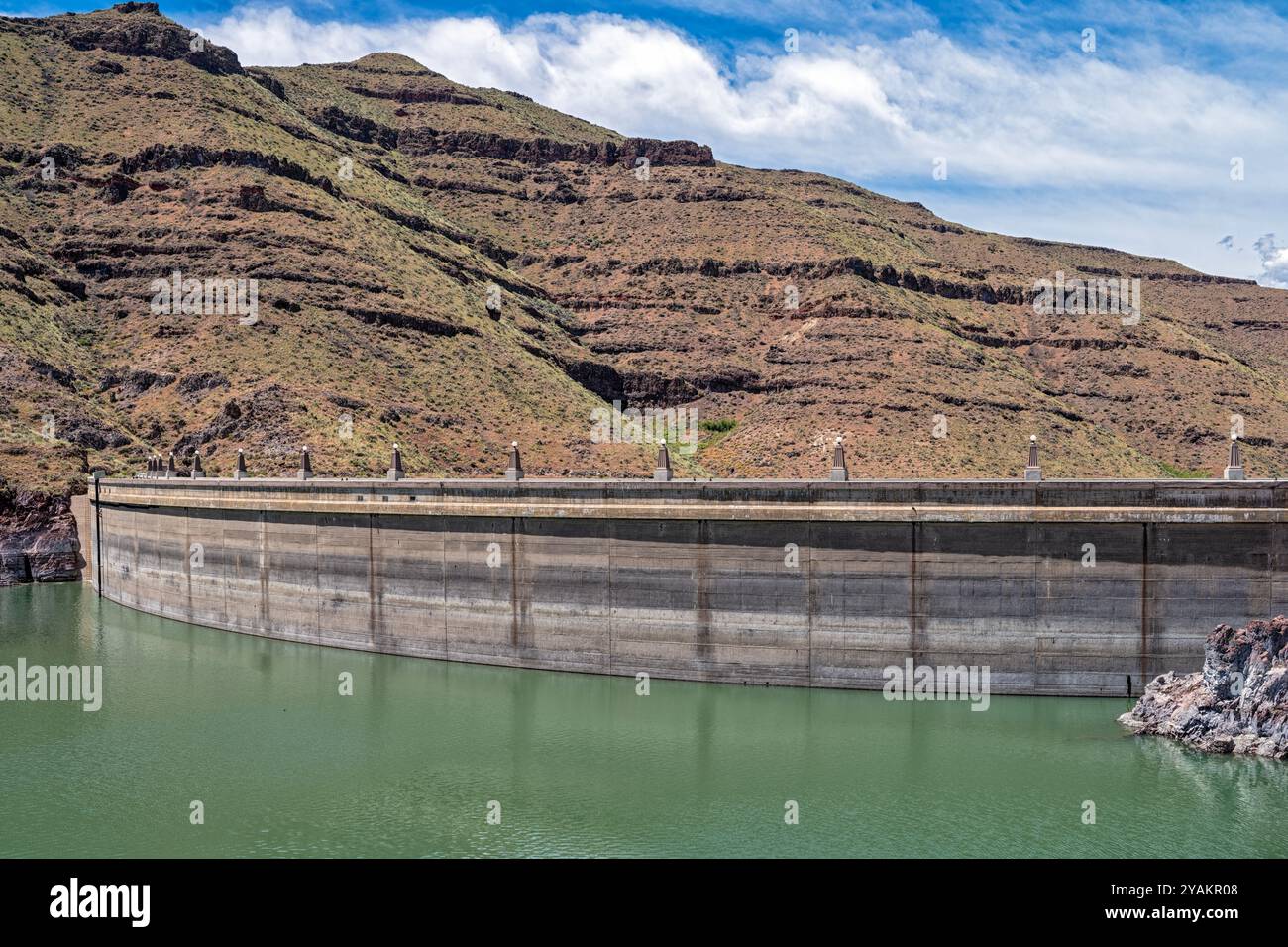 Basalt cliffs rise above the arched concrete wall of the Owyhee dam ...