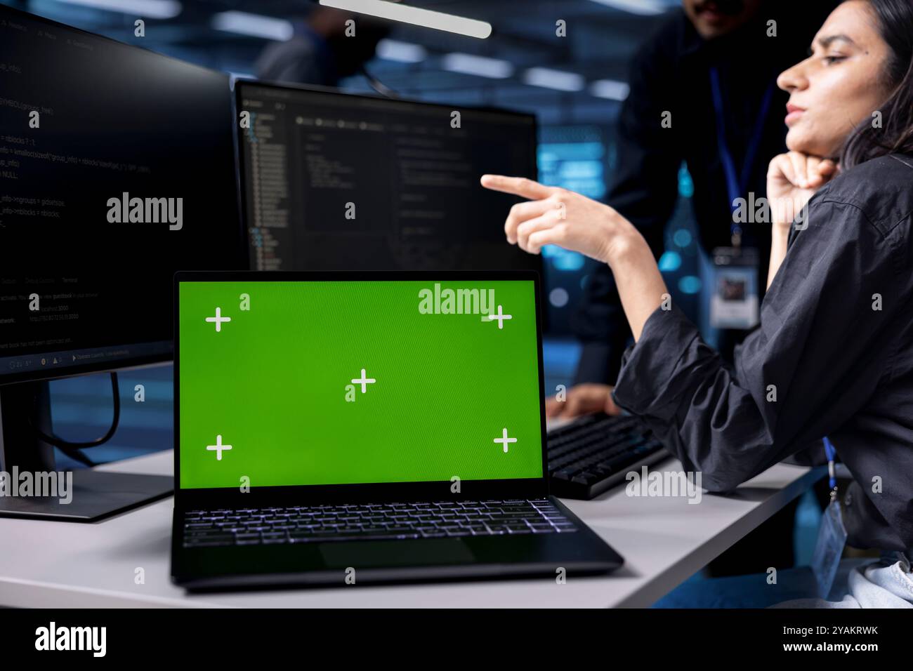 Software developer works on green screen laptop in data center housing storage gear. Worker ...