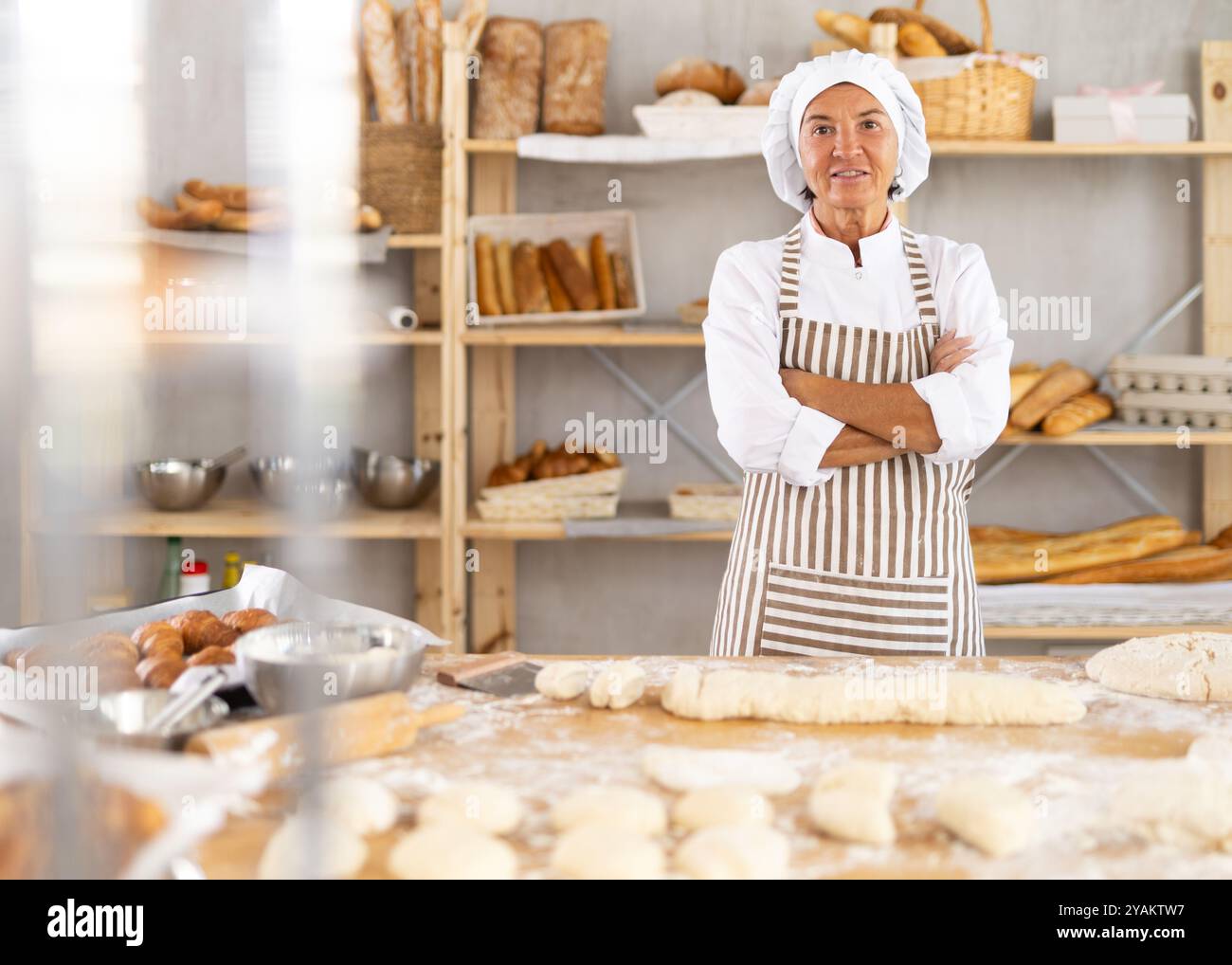 Confident senior female bakery in apron posing with arms crossed ...