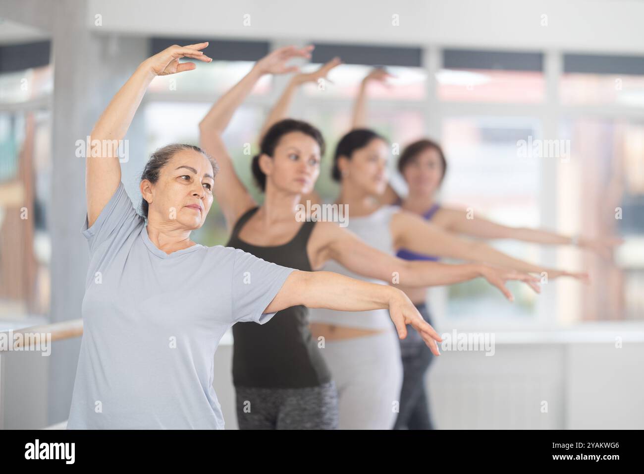 Women of different ages exercise near the ballet barre at group ...