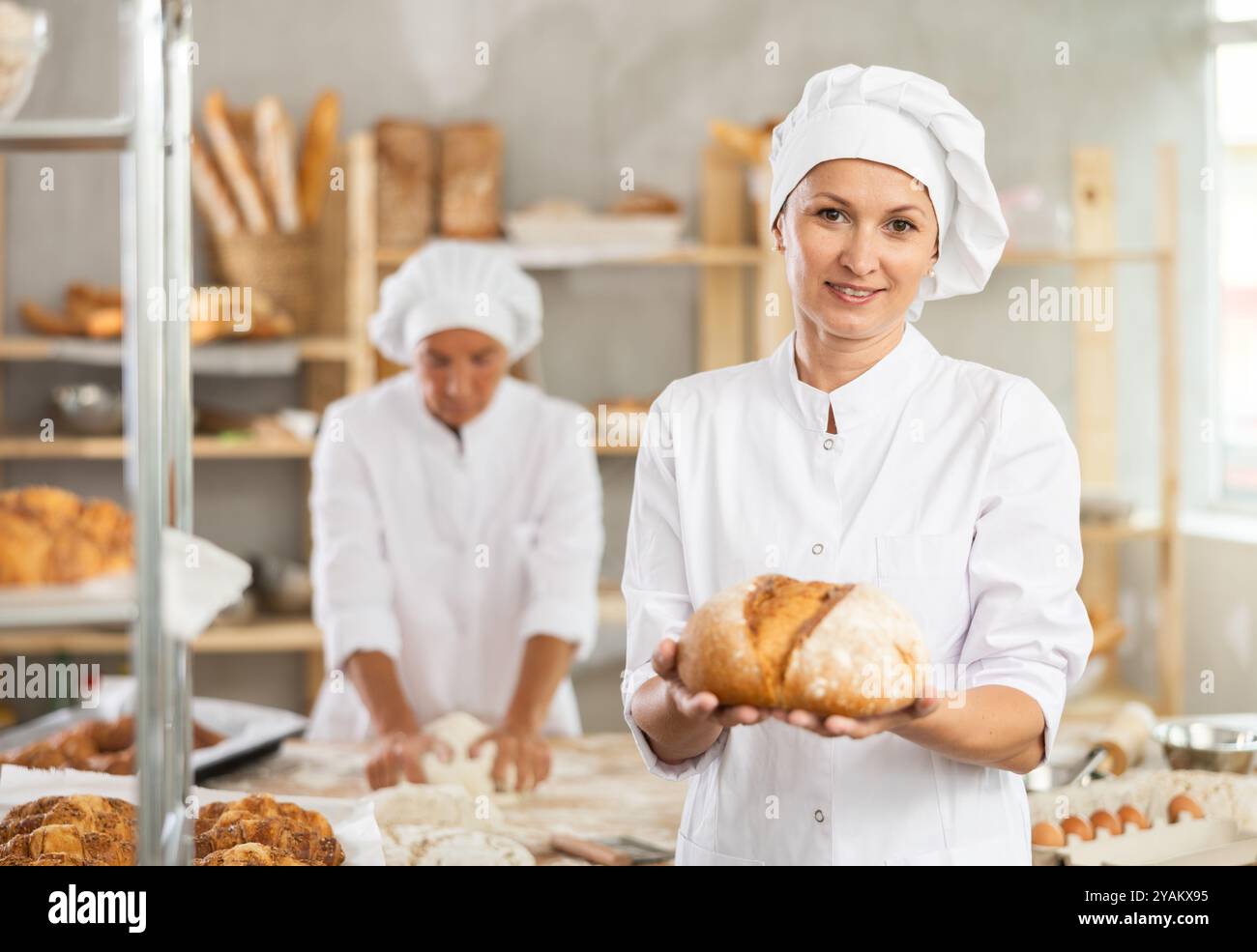 Successful female baker holding fresh bread in cozy bakery Stock Photo ...