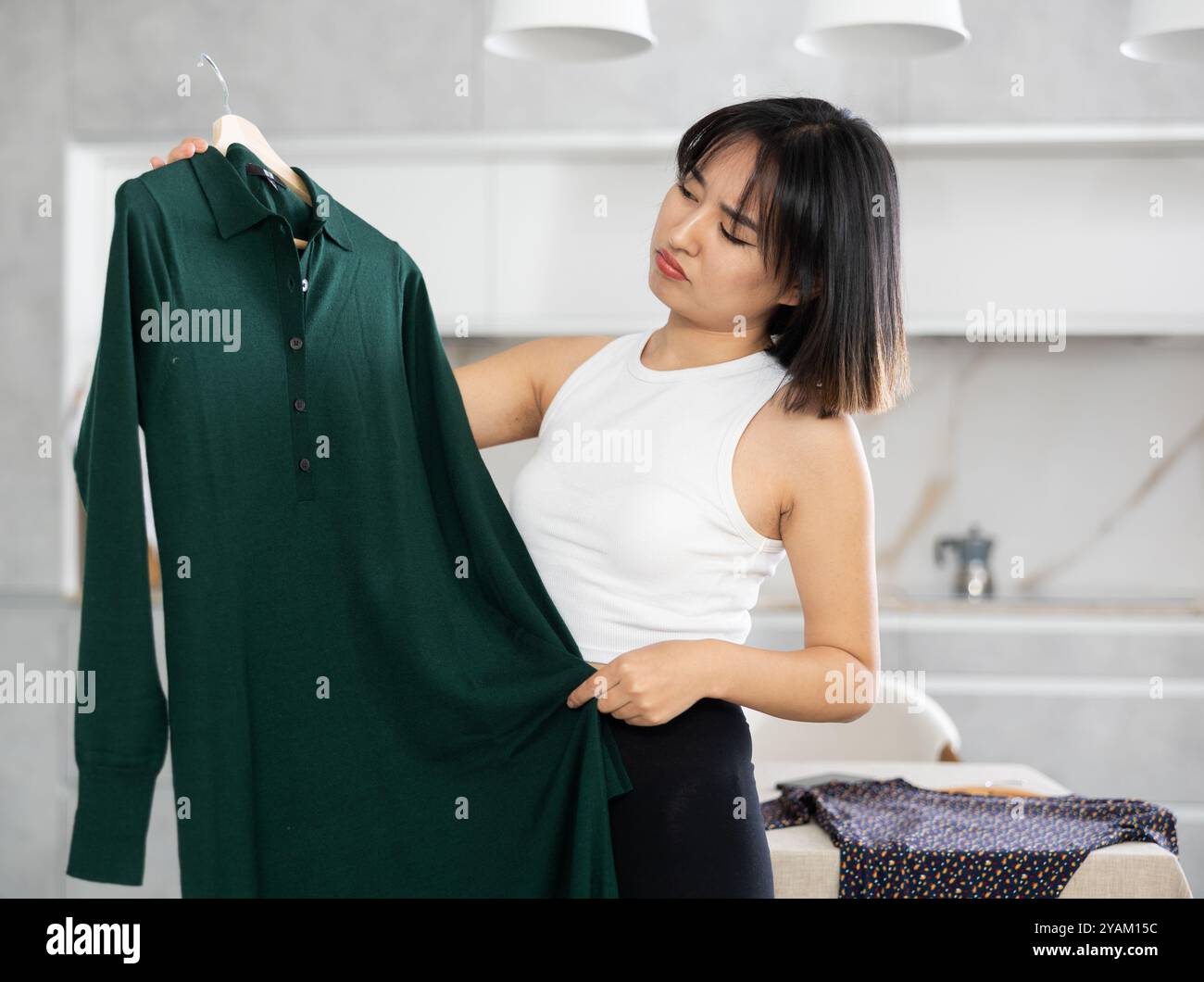 Sad young Asian girl trying to choose a dress in the kitchen Stock ...