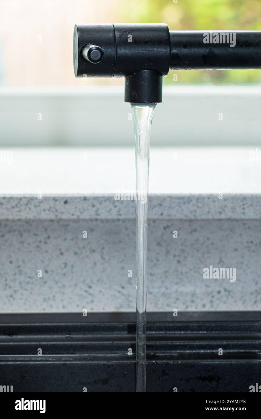 Water is flowing from a black kitchen tap. The tap is in front of a ...