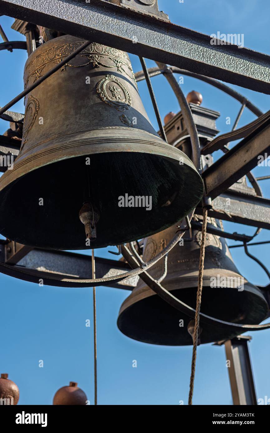 Two ancient bronze bells hang in a church tower against a blue sky ...
