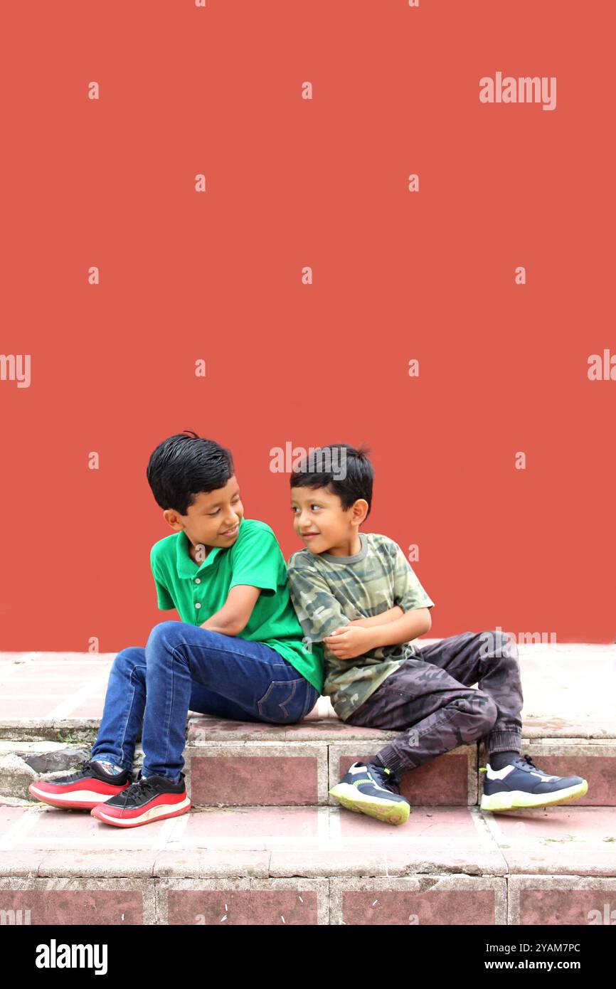 Two dark-haired Latino male children sitting on the ground in a park ...