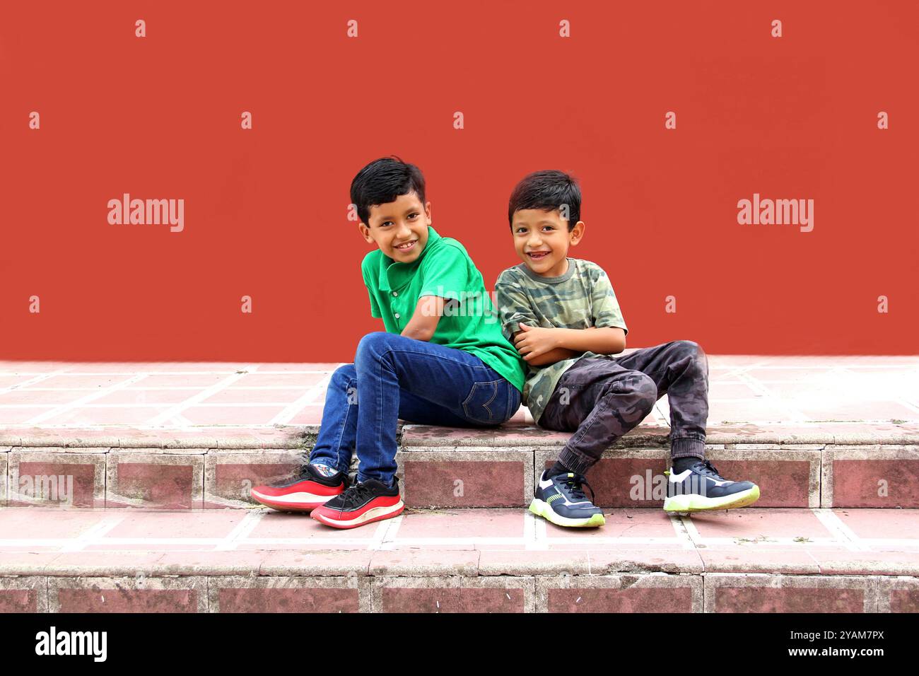 Two dark-haired Latino male children sitting on the ground in a park ...