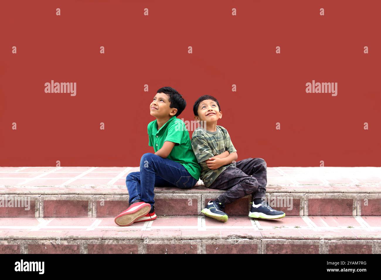 Two dark-haired Latino male children sitting on the ground in a park ...