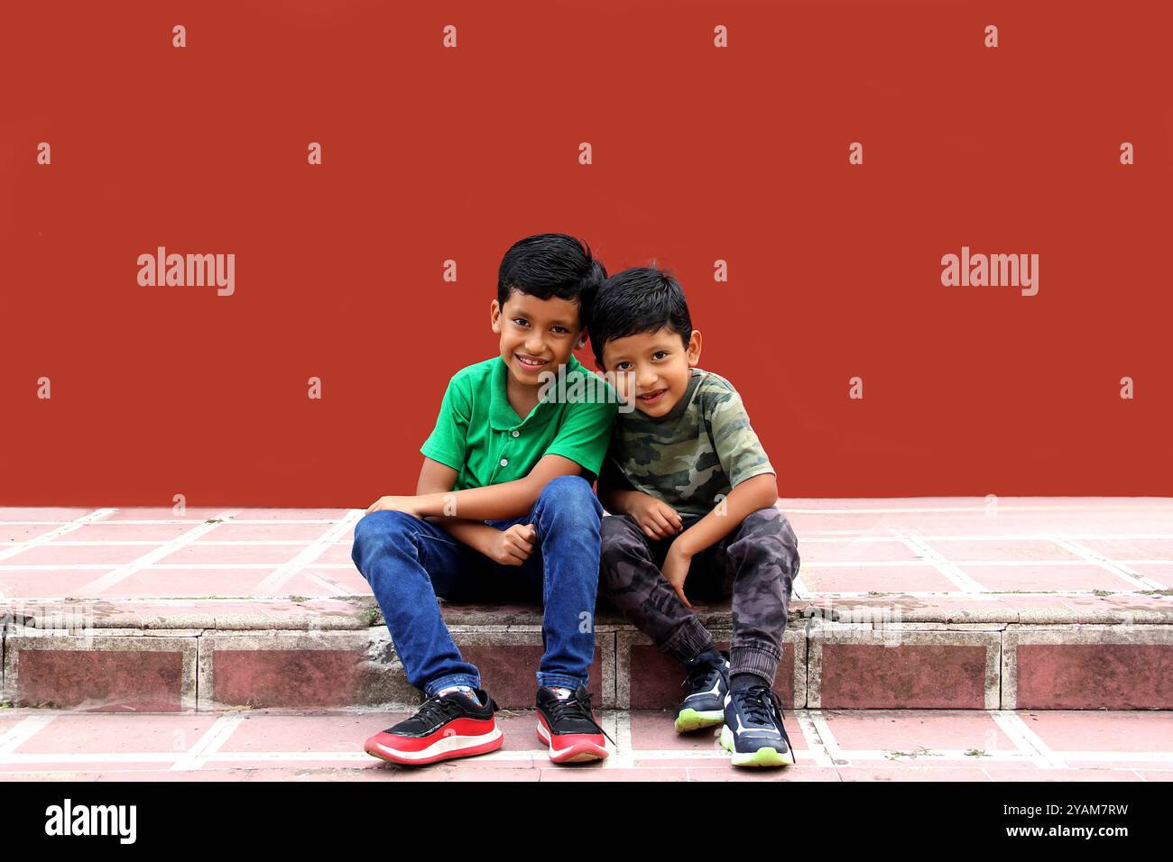 Two dark-haired Latino male children sitting on the ground in a park ...