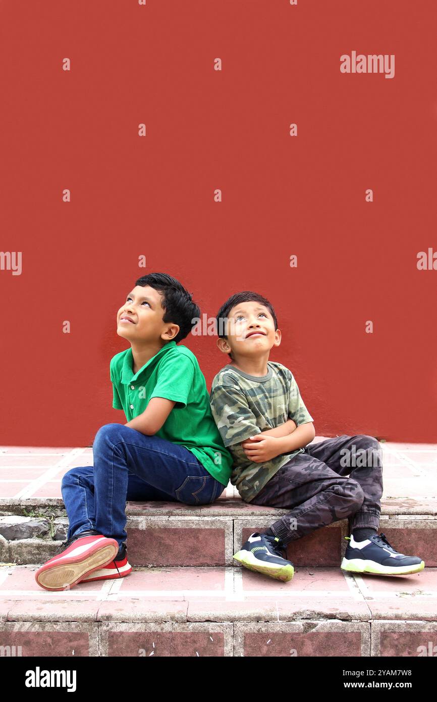 Two dark-haired Latino male children sitting on the ground in a park ...