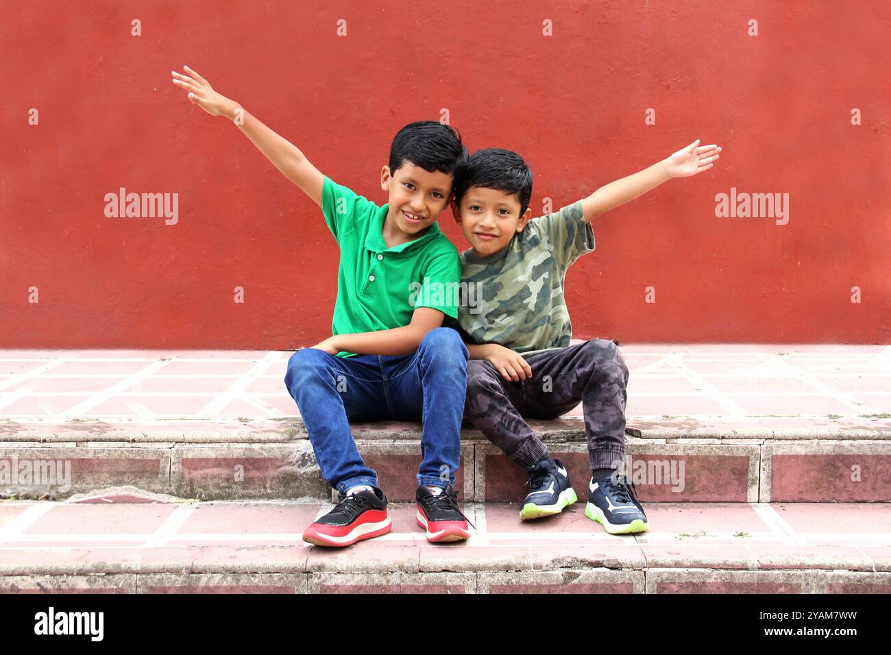 Two dark-haired Latino male children sitting on the ground in a park ...
