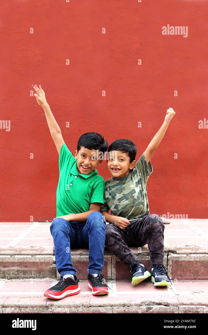 Two dark-haired Latino male children sitting on the ground in a park ...