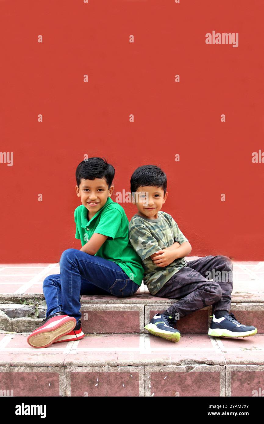 Two dark-haired Latino male children sitting on the ground in a park ...