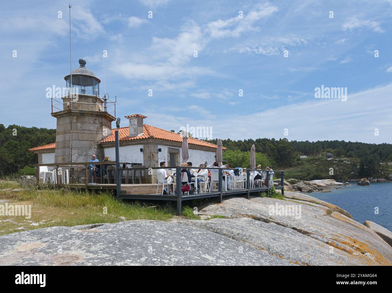 A lighthouse in front of a terrace with people and a view of the sea ...