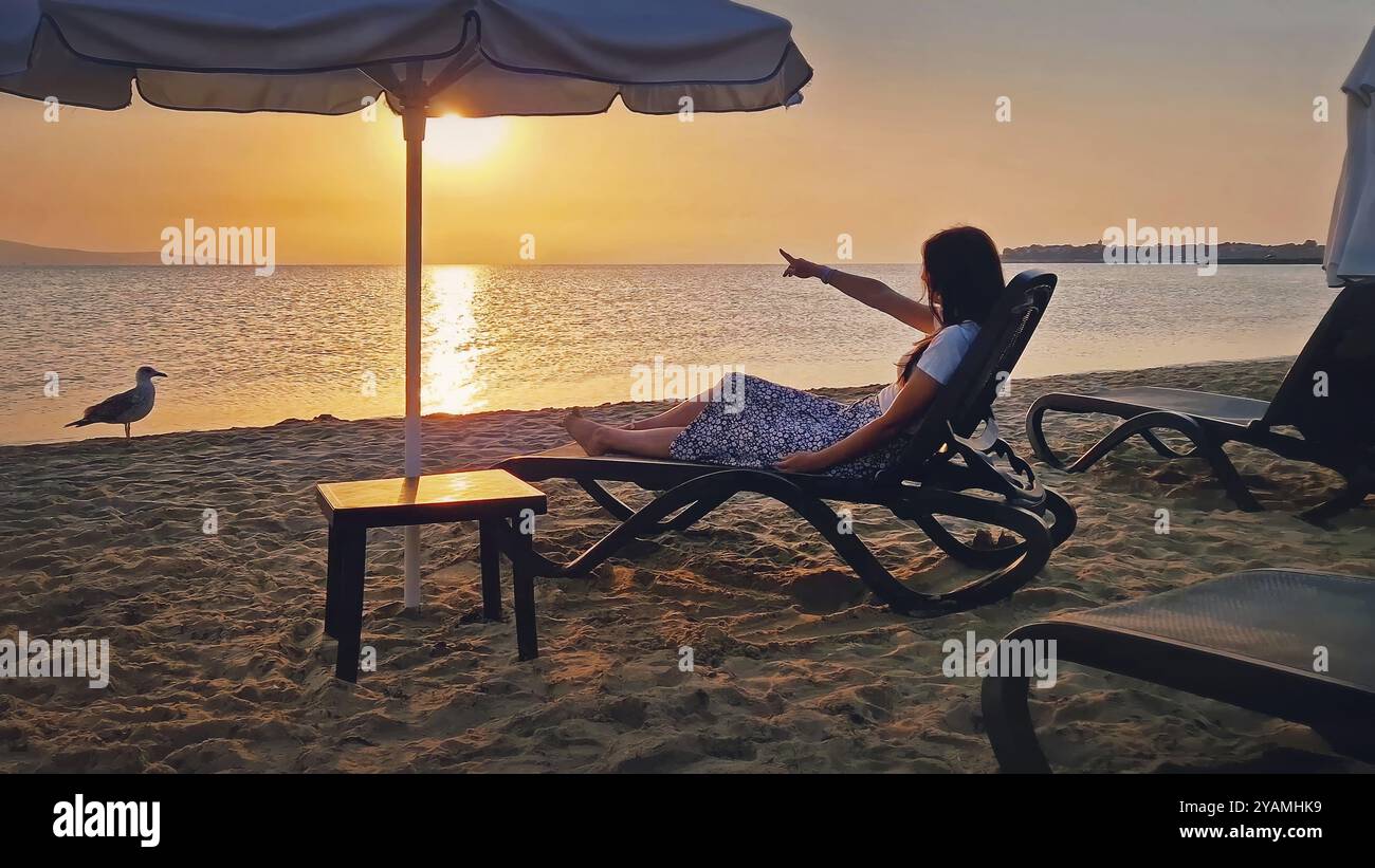 Young woman sitting on a sunbed at the beach pointing forefinger to the ...