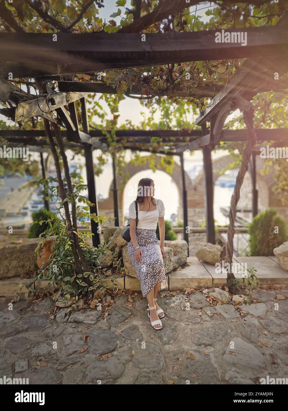Beautiful young woman seated on the stone ruins of the old Nessebar ...