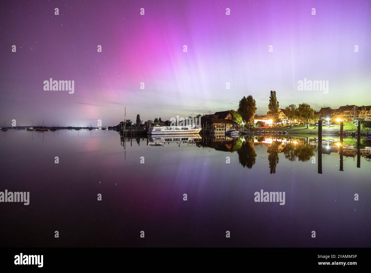 Boats rest in a calm lake while auroras light up the starry sky ...